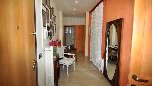 Um corredor com porta de madeira, radiador, mesa com cadeiras e espelho na parede.