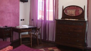 Quarto com escrivaninha de madeira, uma cadeira, cômoda e cama com cobertor roxo.