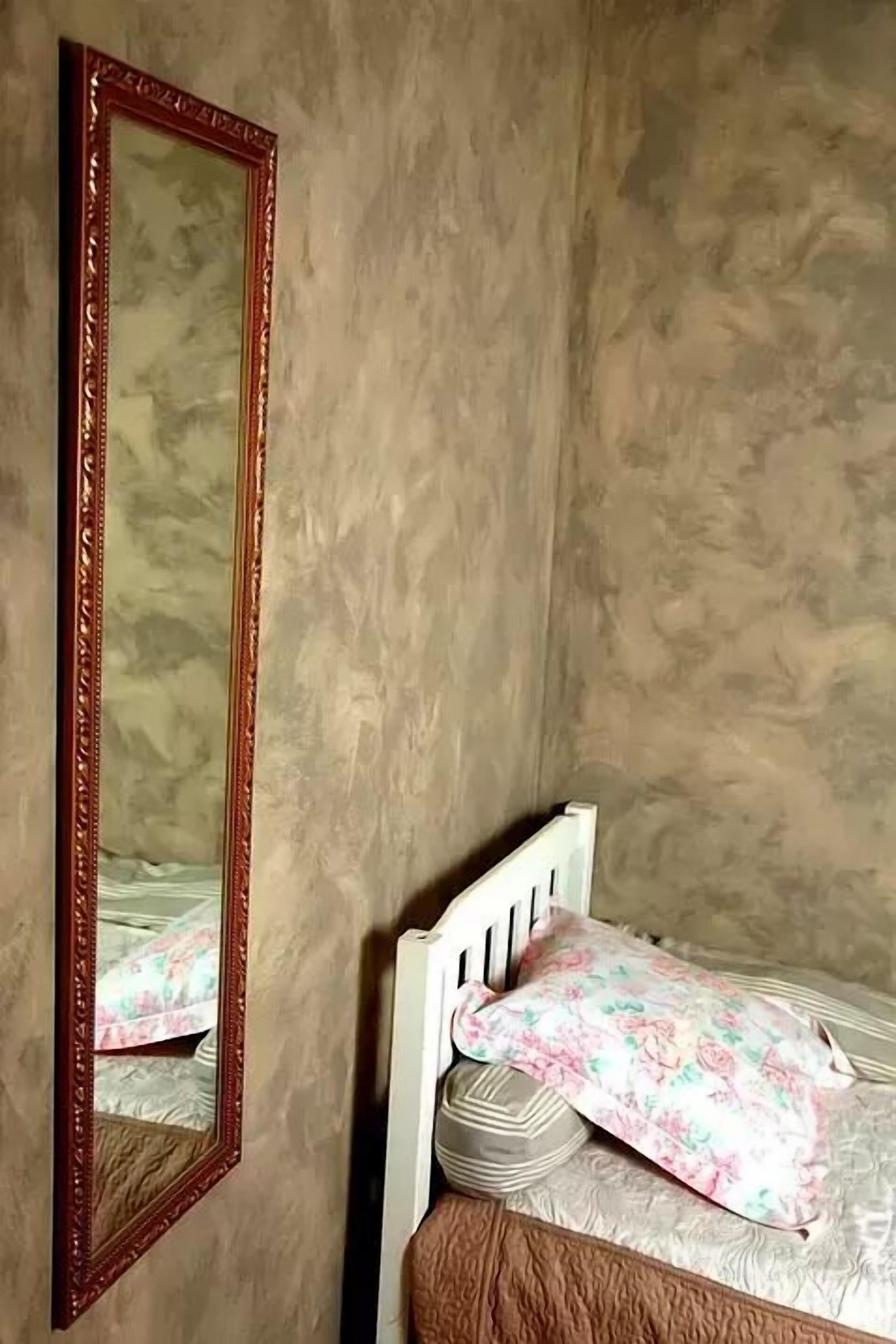 Quarto com cabeceira de madeira, almofada floral e um espelho grande com moldura decorativa.