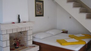 Quarto com lareira de tijolos, cama com roupa de cama branca e cobertores amarelos, cabeceira de madeira e uma escadaria.
