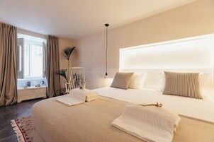 Quarto de hotel com uma cama grande, mesas de cabeceira, uma luminária e vista para o exterior.