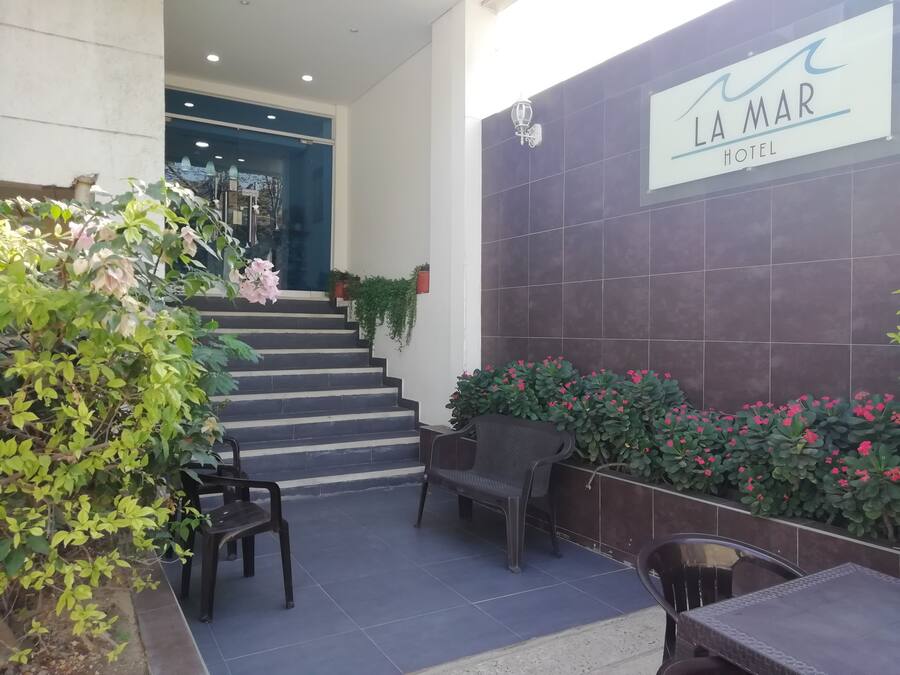 Entrada de um hotel com escadaria que leva ao interior, área de estar ao ar livre com cadeiras e mesas, e uma placa com a inscrição "LA MAR HOTEL".