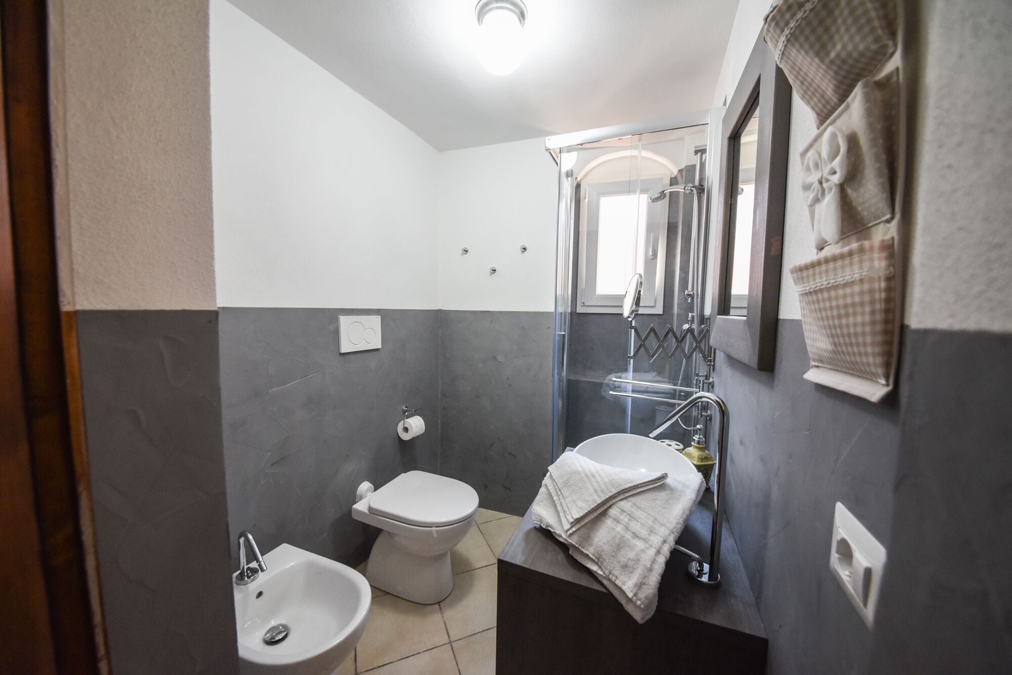 Casa de banho com sanita, bidé, lavatório e cabine de duche em vidro.