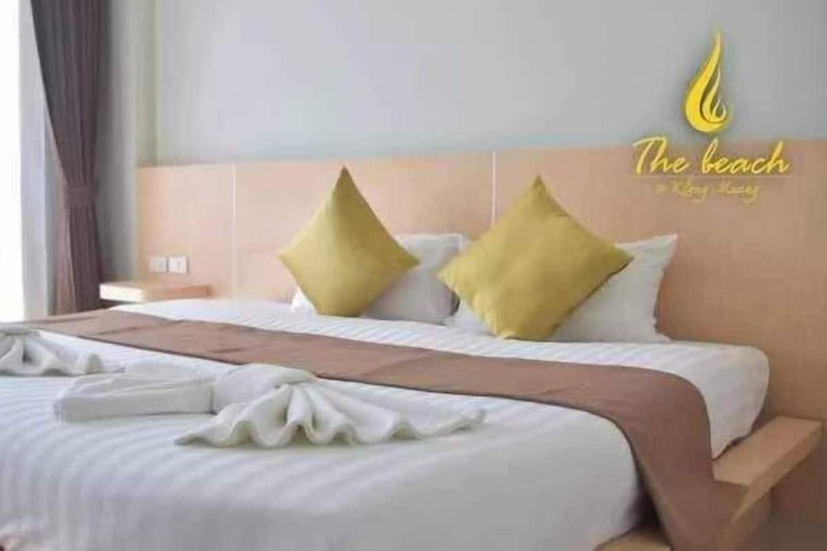 Cama bem arrumada com almofadas, cabeceira de madeira e logo do hotel 'The beach'.