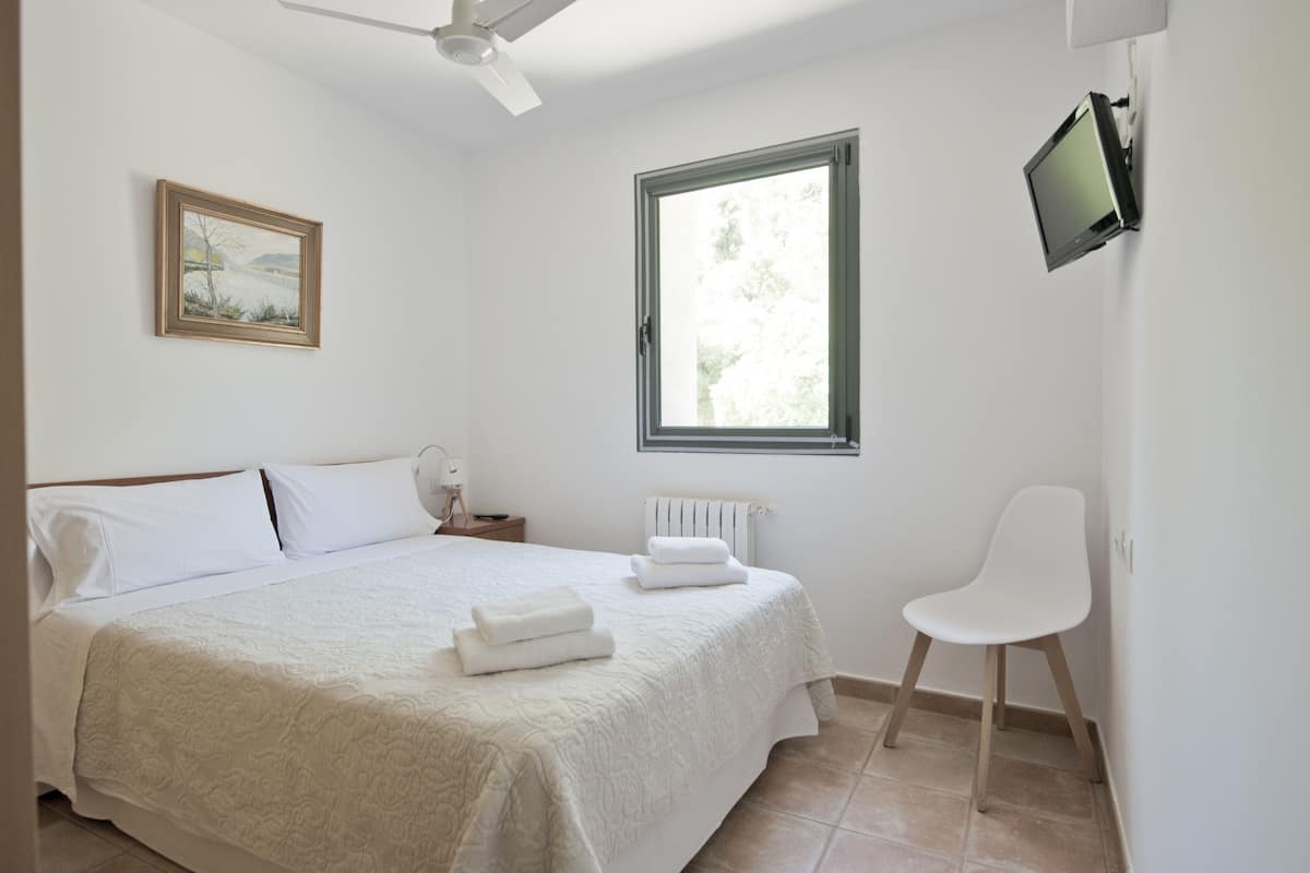 Quarto com uma cama, uma cadeira, uma janela, um quadro e uma televisão.