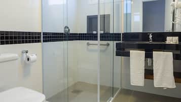 Casa de banho moderna com cabine de duche em vidro, sanita branca e bancada preta com espelho e porta-toalhas.
