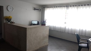 Uma área de recepção com balcão, relógio, televisão e uma janela com cortinas.