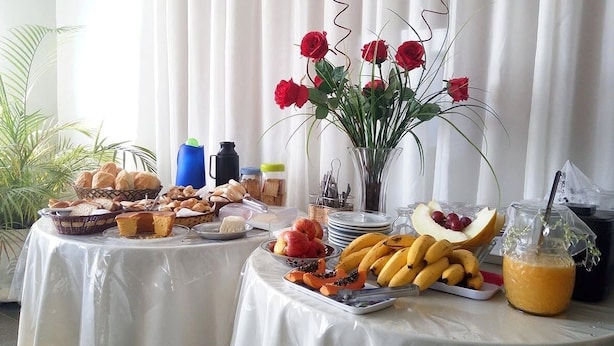 Uma mesa de buffet com diversos alimentos e um vaso de rosas vermelhas.