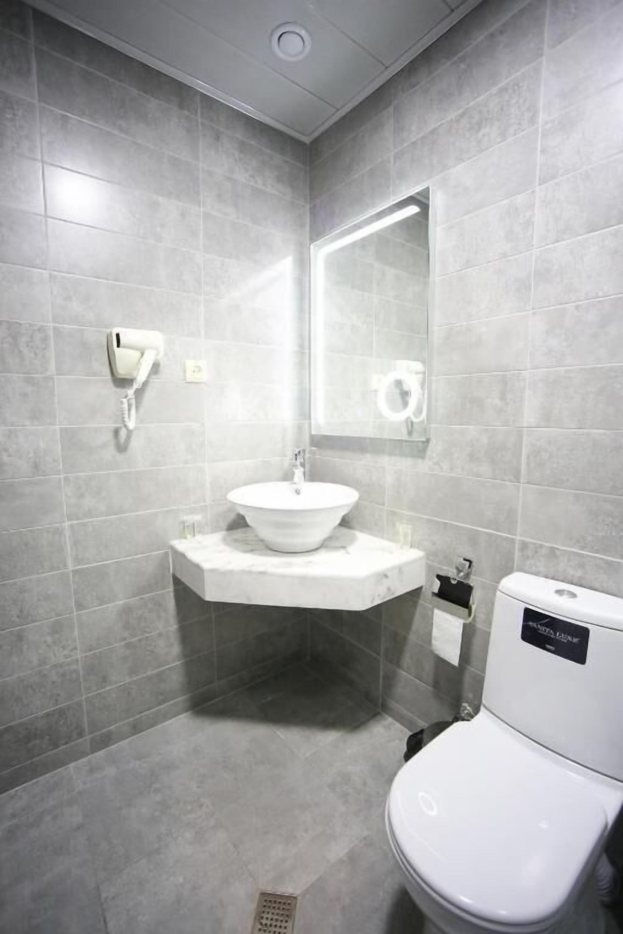 Um banheiro moderno com azulejos cinzas, pia branca, espelho e vaso sanitário.