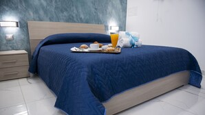 Uma cama bem arrumada com um edredom azul, um tabuleiro com croissants, uma chávena de café e um copo de sumo de laranja.