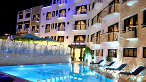 Um hotel com piscina, espreguiçadeiras e área externa coberta.