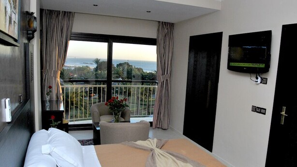Quarto de hotel com cama, poltrona, televisão e varanda vista para o mar.