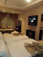 Quarto de hotel com duas camas, uma televisão na parede, uma mesinha e um sofá.