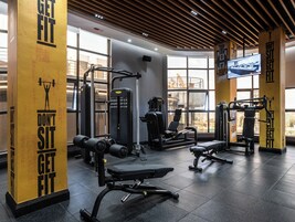 Uma academia com diversos equipamentos de exercícios, amplas janelas e adesivos motivacionais nas paredes.