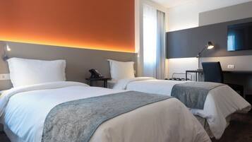 Quarto de hotel com duas camas, uma escrivaninha, uma cadeira, uma televisão e um telefone no criado-mudo.