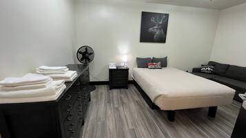 Quarto moderno com cama, penteadeira, mesa de cabeceira, ventoinha e uma obra de arte na parede.