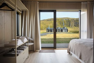 Quarto com uma grande porta de vidro deslizante que dá para uma área externa panorâmica com cachoeira e colinas.