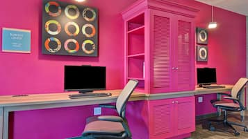 Um espaço de trabalho com duas mesas, duas cadeiras, um armário rosa e uma obra de arte na parede.