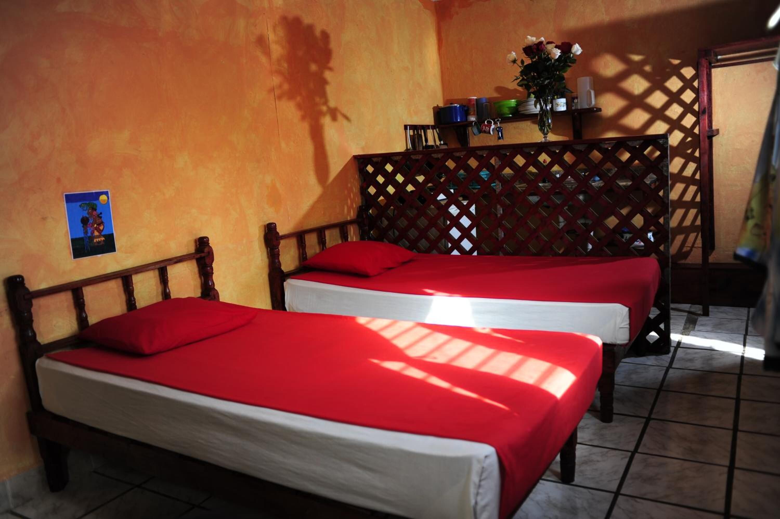 Quarto com duas camas, cabeceira de madeira, prateleira com utensílios de cozinha e parede com um pôster.
