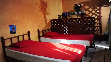 Quarto com duas camas, cabeceira de madeira, prateleira com utensílios de cozinha e parede com um pôster.