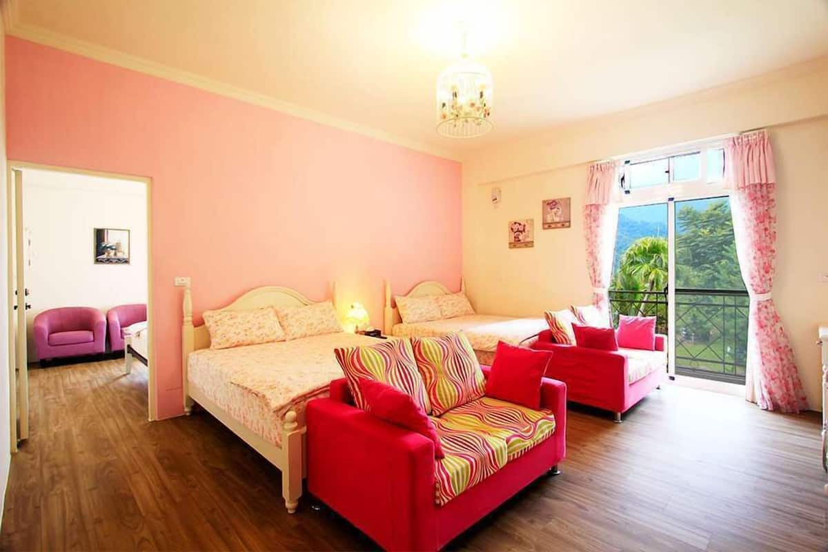 Quarto com duas camas, um sofá vermelho e uma varanda com cortinas.