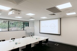 Uma sala de conferências com uma mesa comprida, cadeiras, tela de projetor e quadro branco.