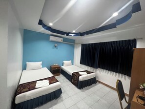 Quarto de hotel com duas camas, uma escrivaninha, uma cadeira, uma janela com cortinas e um aparelho de ar condicionado.