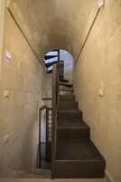Uma escadaria estreita com paredes de pedra e corrimão de metal.