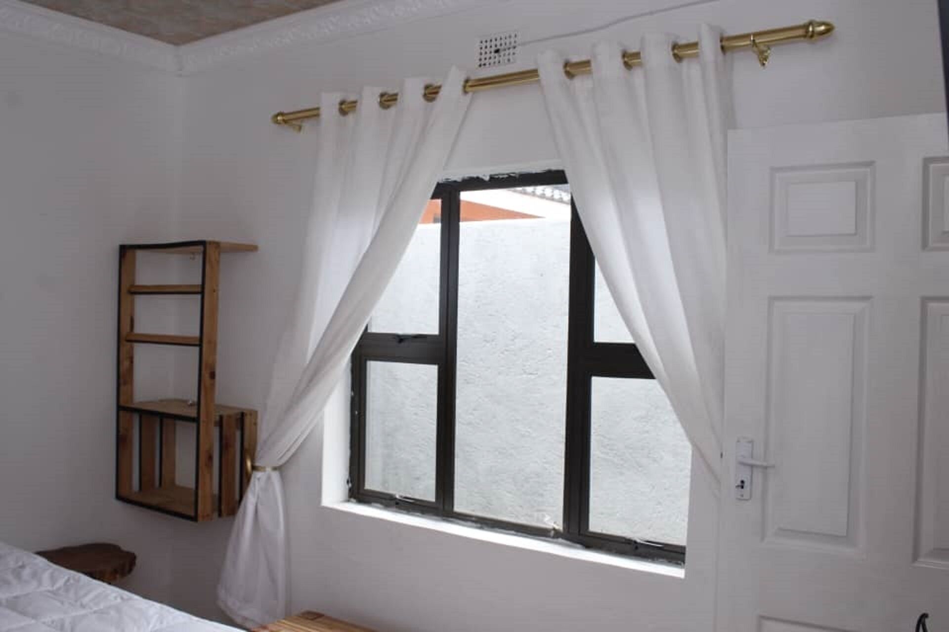 Um quarto com janela, prateleira de madeira e porta branca.
