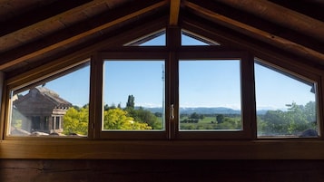 Quarto com teto inclinado e grandes janelas que oferecem vista para um edifício distante e paisagem.