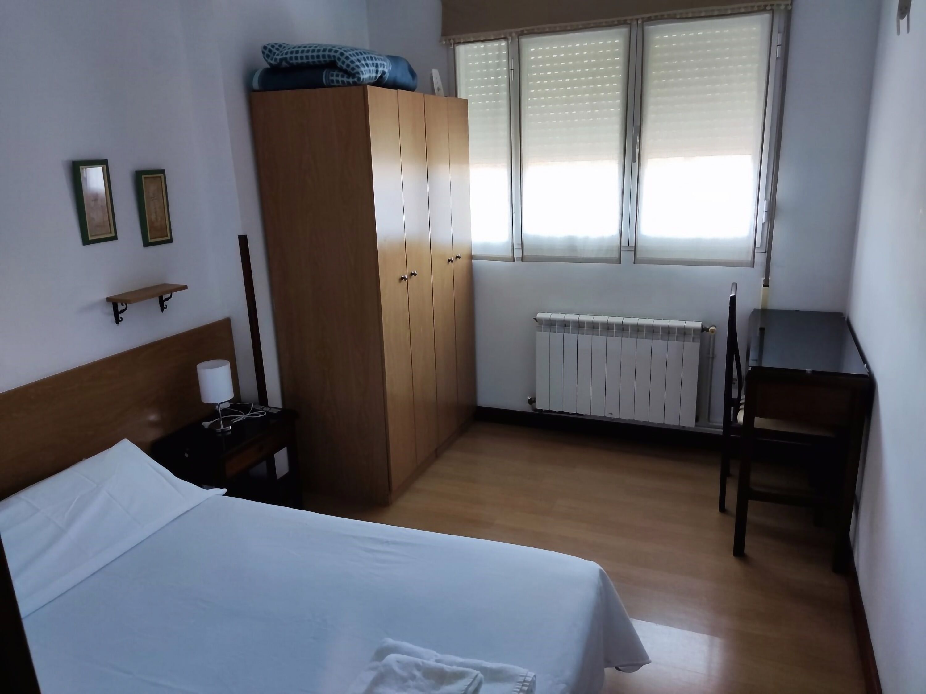 Quarto com cama, guarda-roupa, escrivaninha e radiador.