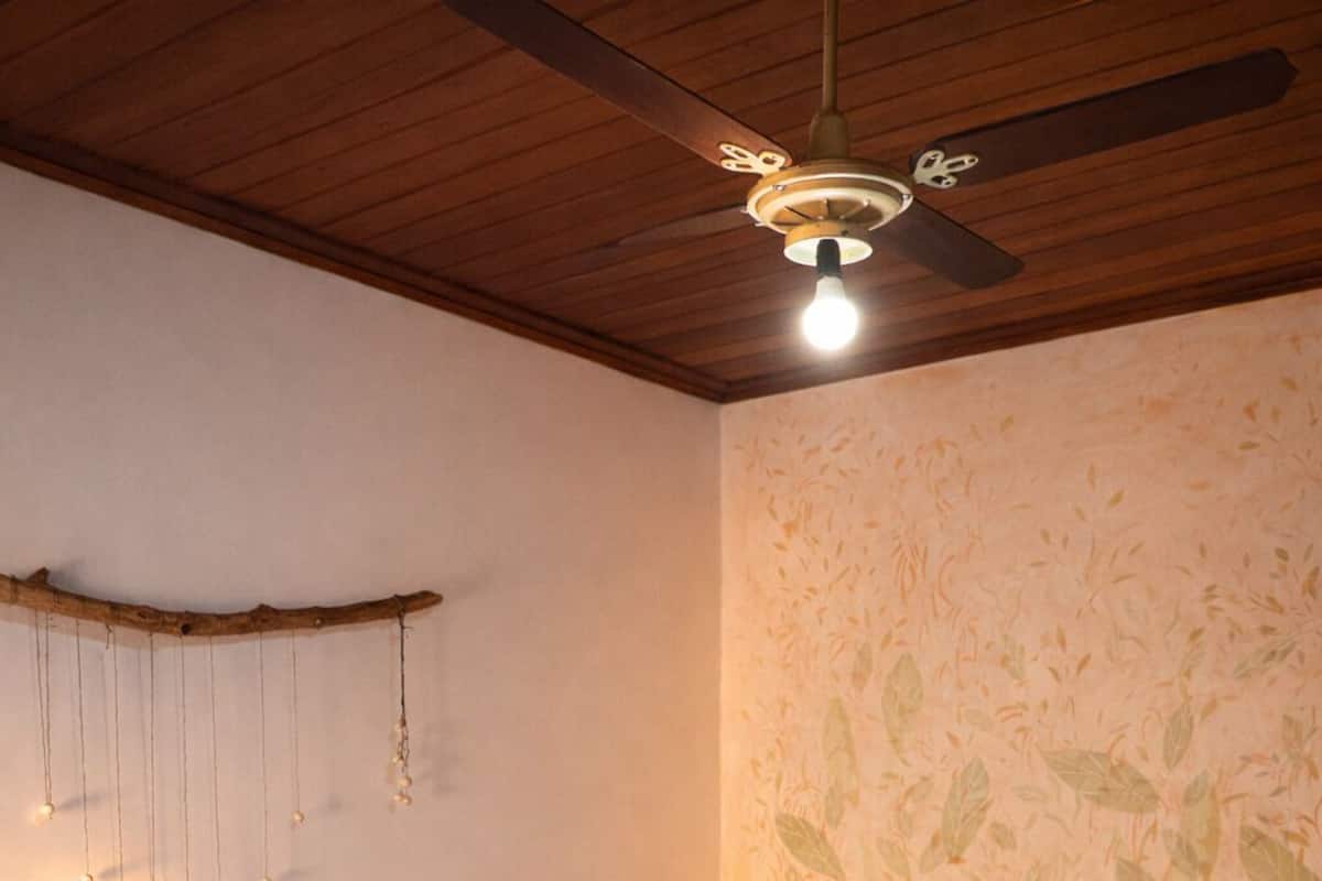 Quarto com cama de madeira, luminária pendente e papel de parede floral.