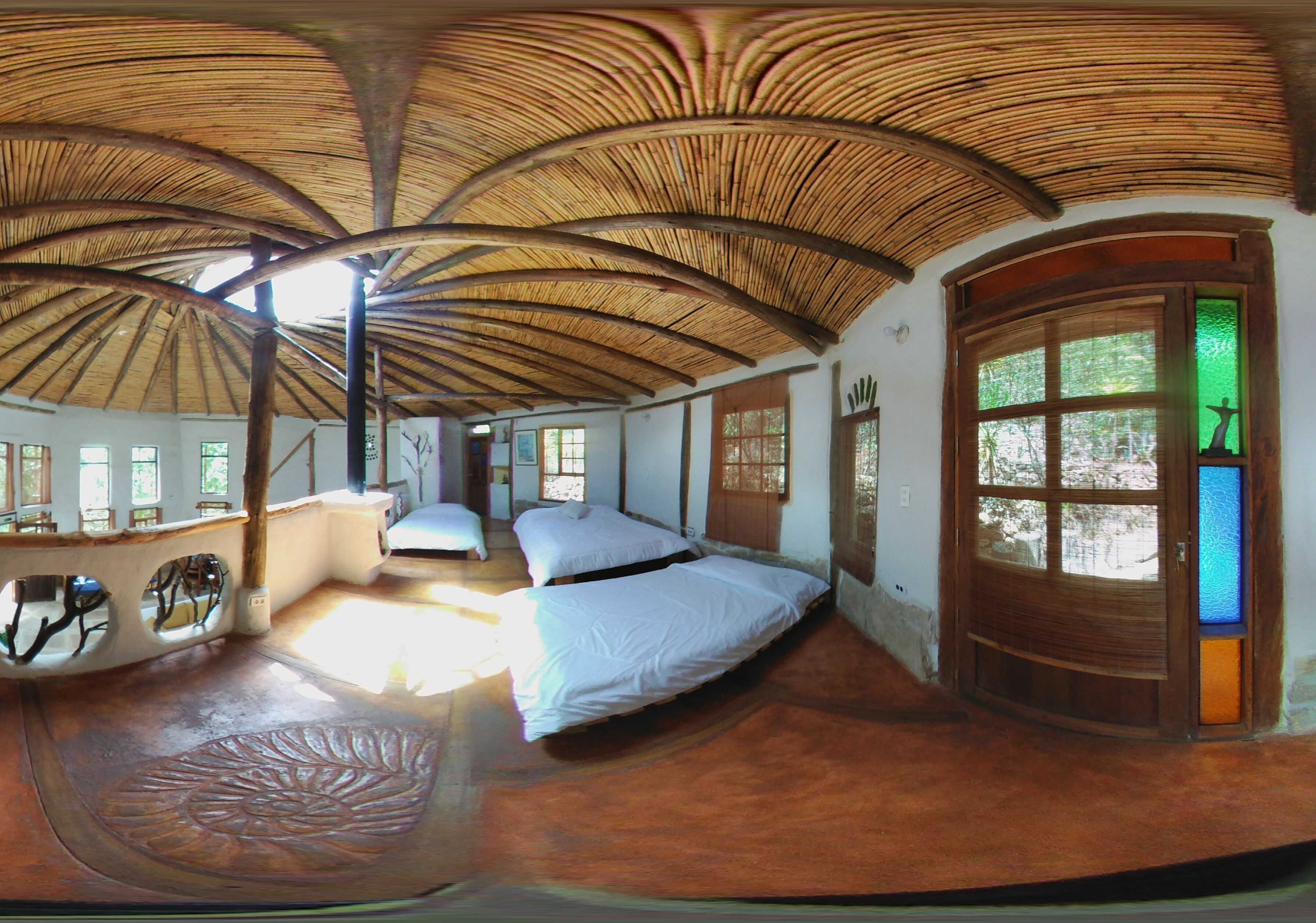 Quarto com telhado de palha, uma cama, uma mesinha e janela com vista para o verde.