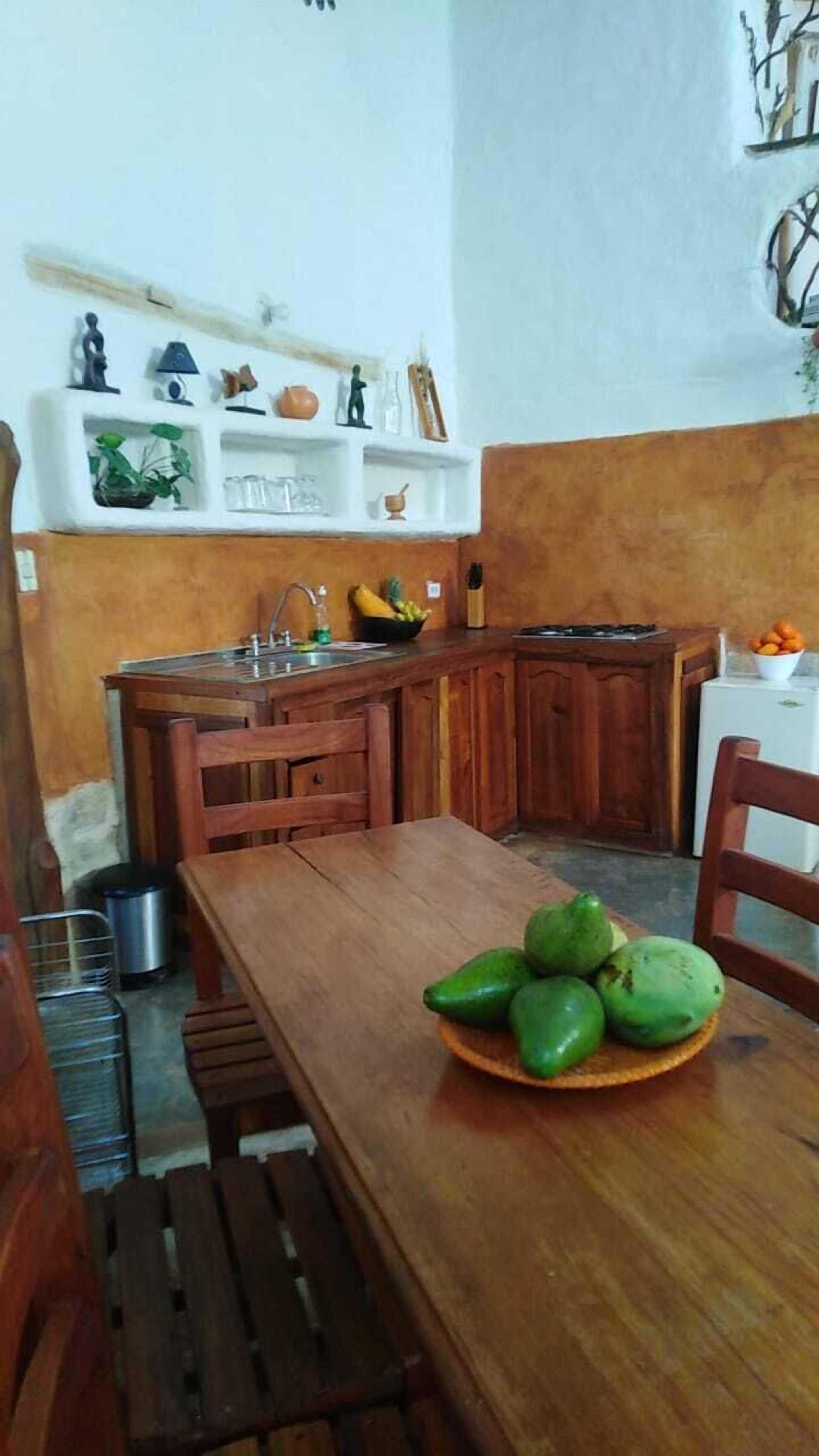Uma cozinha com armários de madeira, uma mesa de jantar com uma tigela de frutas verdes e uma geladeira branca.