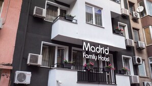 Um edifício com várias andares, varandas, aparelhos de ar condicionado e uma placa com o nome Madrid Family Hotel.