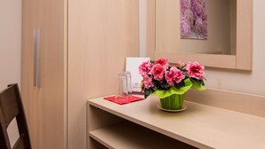 Uma mesa de madeira com um vaso de flores cor-de-rosa, um guardanapo vermelho e um copo de água.