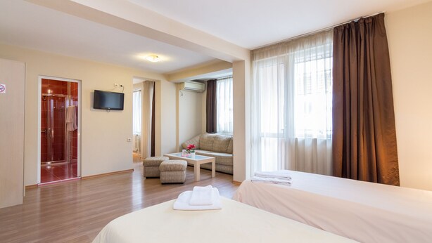 Quarto de hotel com cama, sofá, mesinha e televisão.