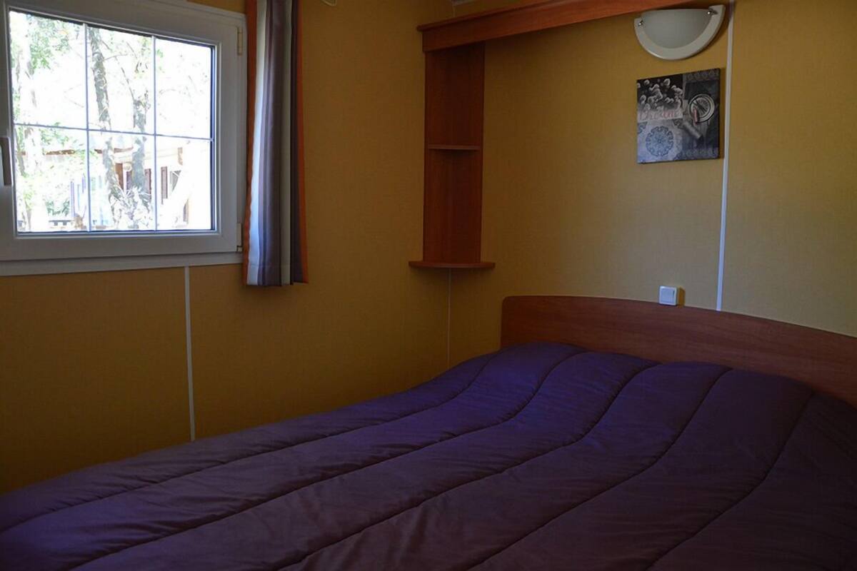 Quarto com cama, janela, prateleira na parede e relógio de parede.