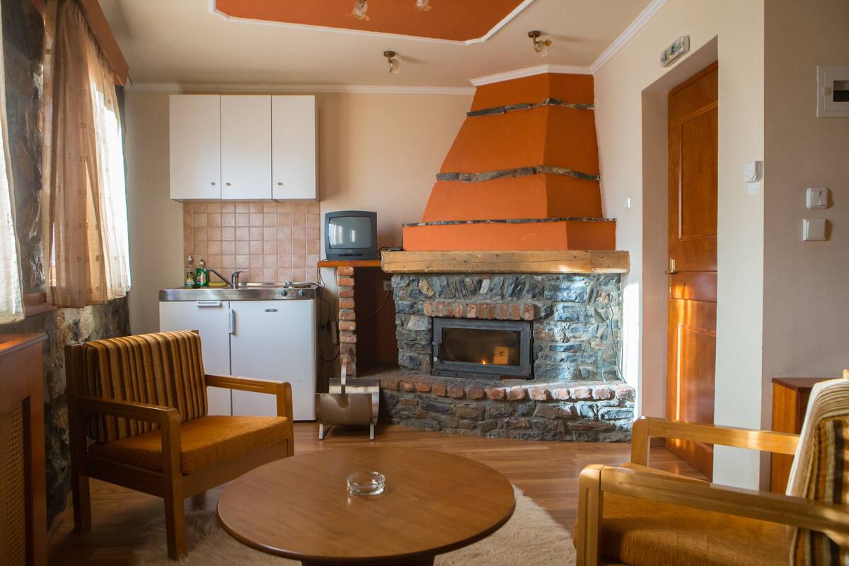 Uma sala de estar aconchegante com lareira, móveis de madeira e uma área de cozinha com armários e uma televisão.