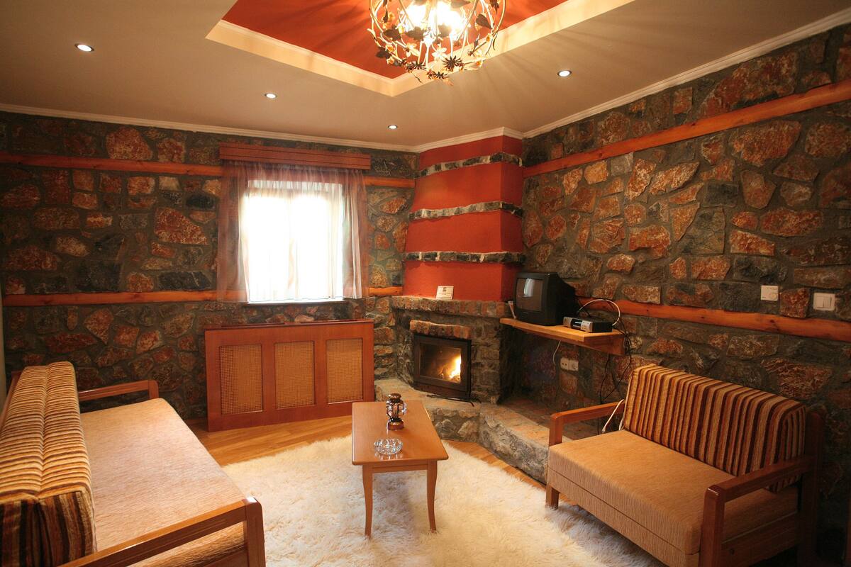 Uma sala de estar aconchegante com lareira de pedra, móveis de madeira e uma grande janela com cortinas.