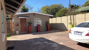 Uma casa pequena, térrea, com porta de madeira, uma janela e dois grandes vasos.