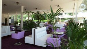 Um espaço de refeições interno com assentos brancos e roxos, grandes janelas e ventiladores de teto.
