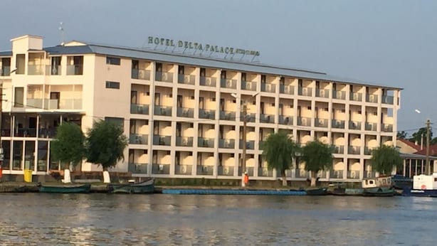 Um hotel com vários andares, varandas, uma placa com a inscrição 'HOTEL DELTA PALACE' e vista para a orla marítima.