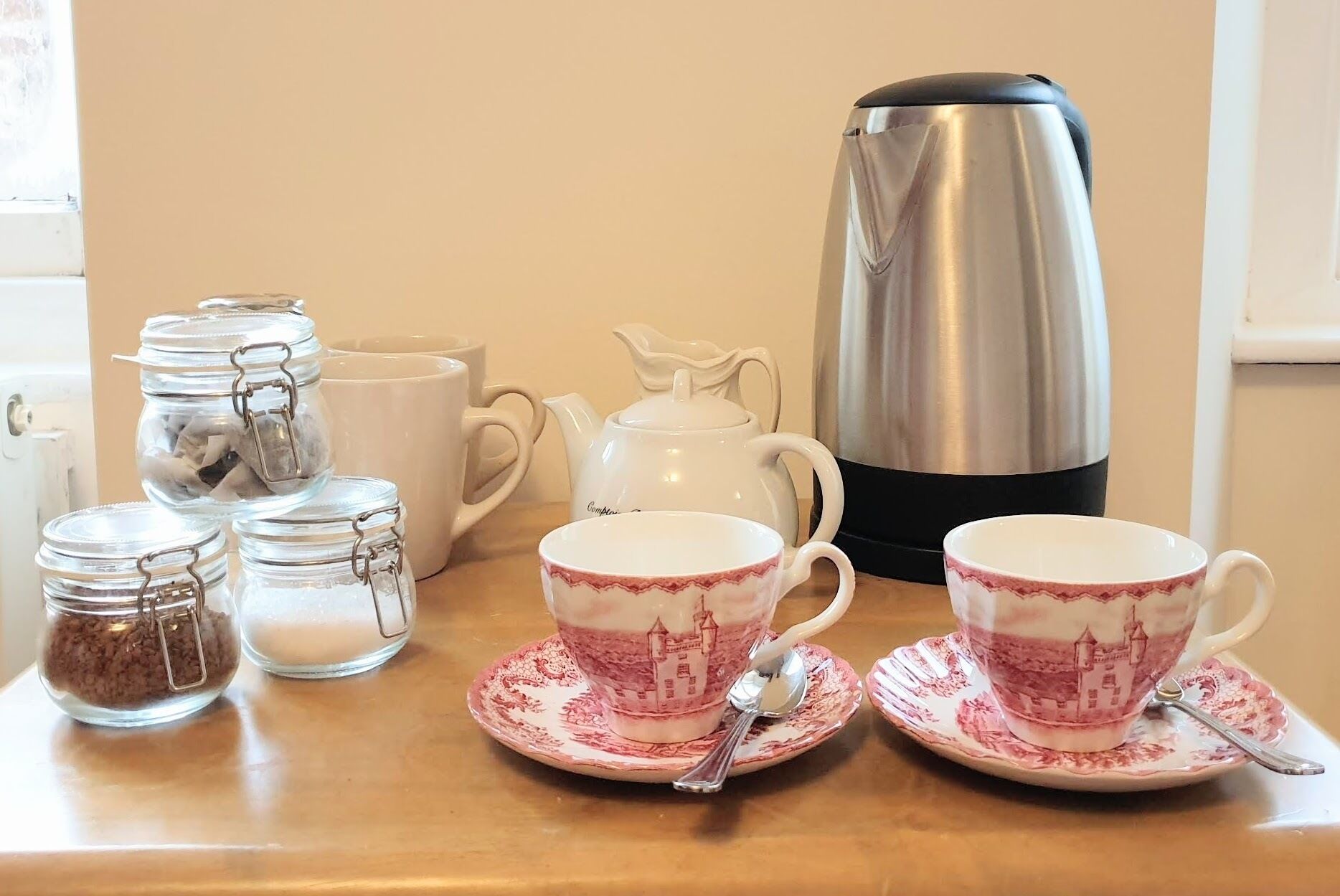 Uma mesa com duas xícaras, um bule, um açucareiro e dois potes de vidro.