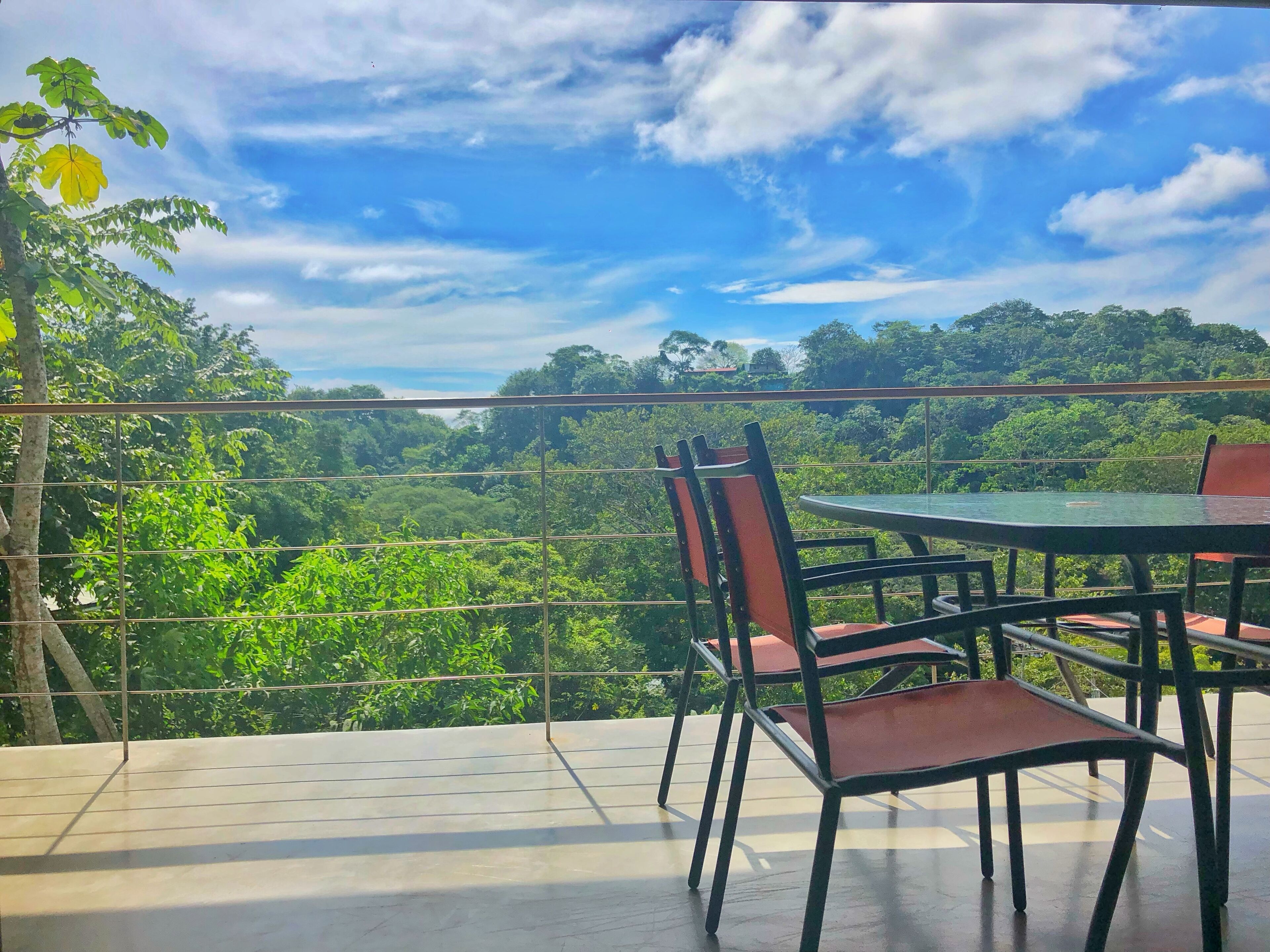 Um terraço com mesa e cadeiras, com vista para uma paisagem verde exuberante.