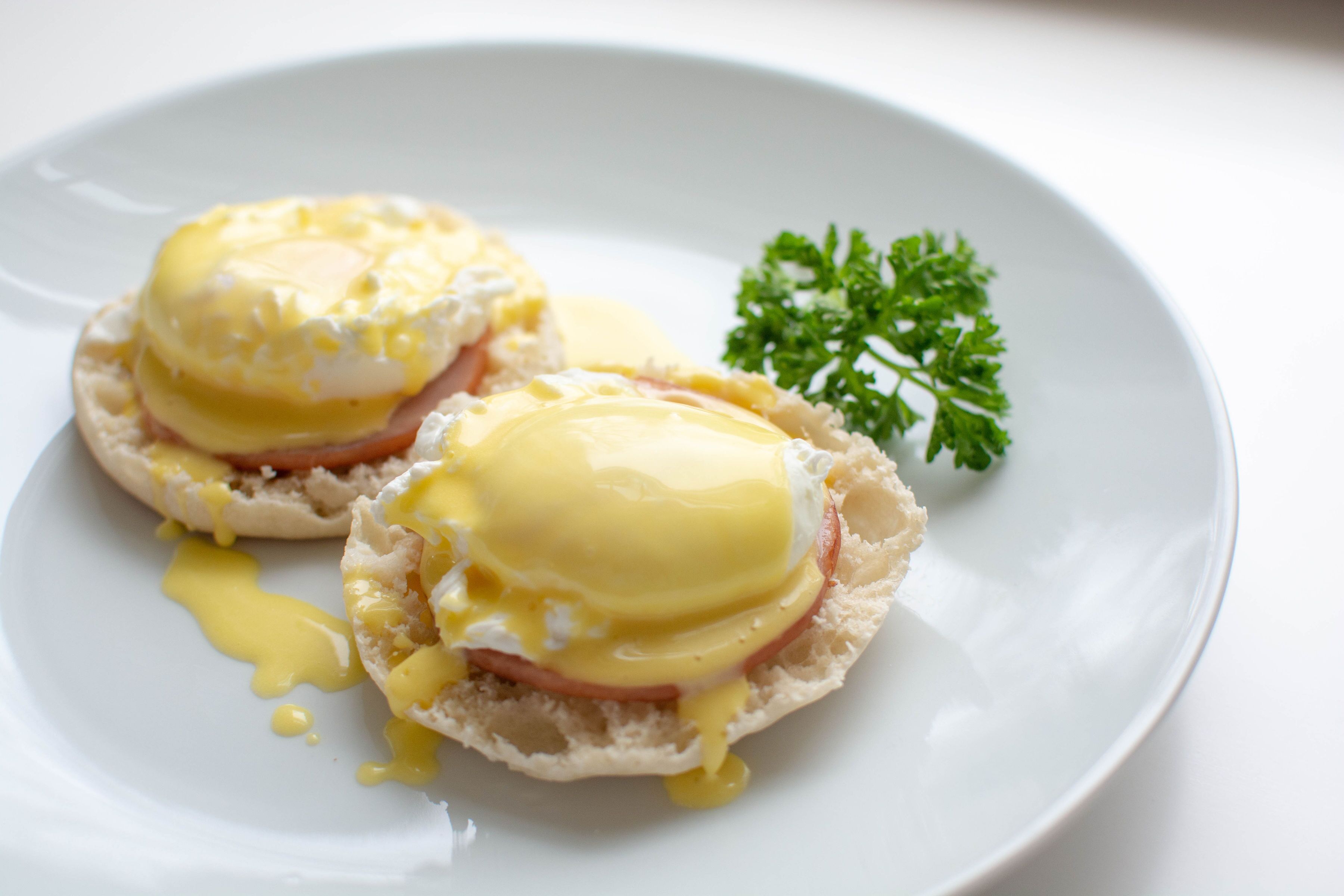 Dois sanduíches eggs benedict em um prato branco, com enfeite de salsa.