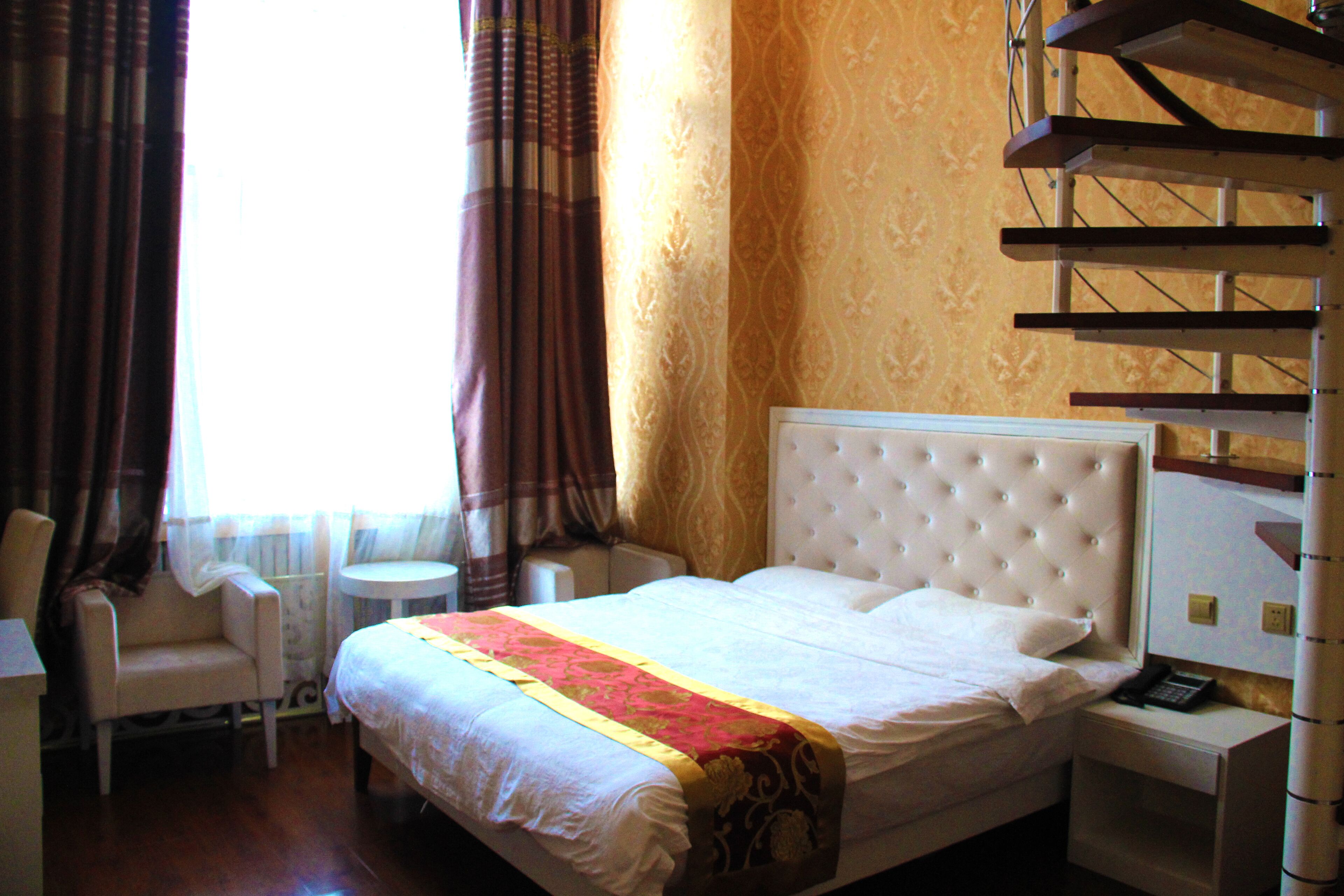 Quarto de hotel com cama, poltrona, mesa pequena e escrivaninha.
