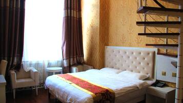 Quarto de hotel com cama, poltrona, mesa pequena e escrivaninha.