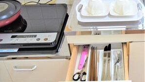 Cozinha com fogão, micro-ondas e bandeja com bules. Utensílios e um bloco de facas rosa estão à vista.