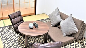 Um quarto com piso de tatame, um sofá marrom baixo com almofadas, uma poltrona de couro marrom e uma pequena mesa redonda com um bule e duas xícaras.